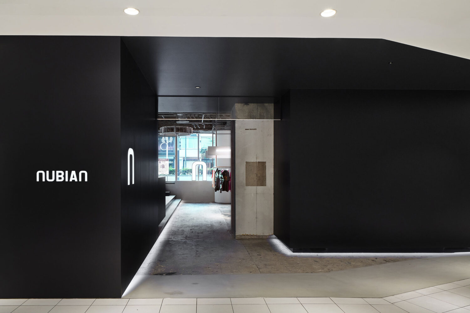 トラフによる、名古屋市の店舗「NUBIAN NAGOYA PARCO」。商業施設の内と外に入口がある区画に計画。環境条件の空間演出への援用を目指し、内では視界を絞り入店体験を設計して外では高低 ...